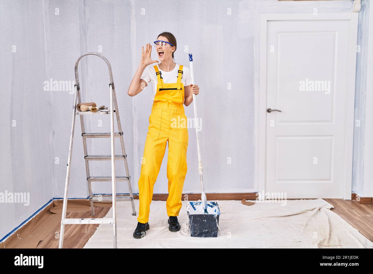 Young caucasian woman painting walls shouting and screaming loud to ...