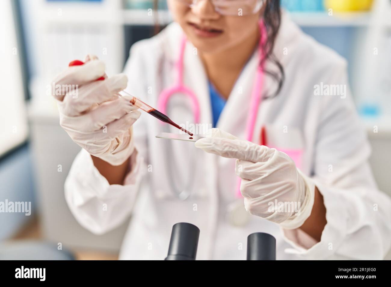 Young chinese woman wearing scientist uniform analysing blood at ...