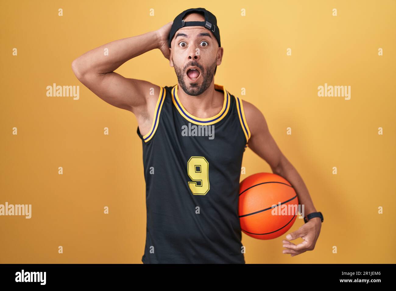 Middle age bald man holding basketball ball over yellow background ...