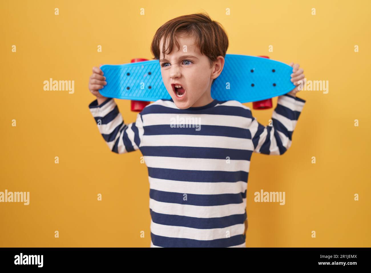 Little caucasian boy holding skate over yellow background angry and mad ...