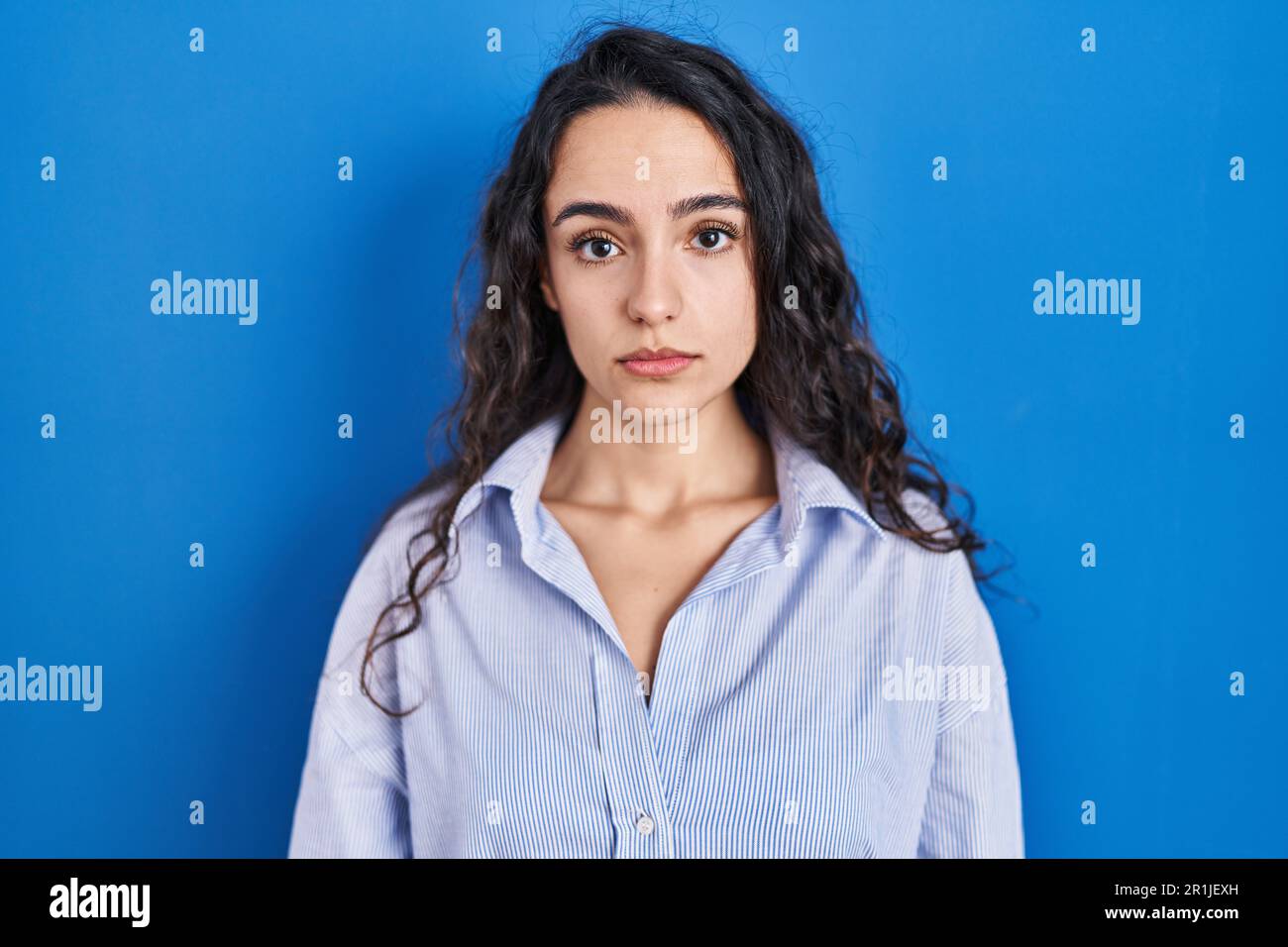 Young brunette woman standing over blue background depressed and worry ...