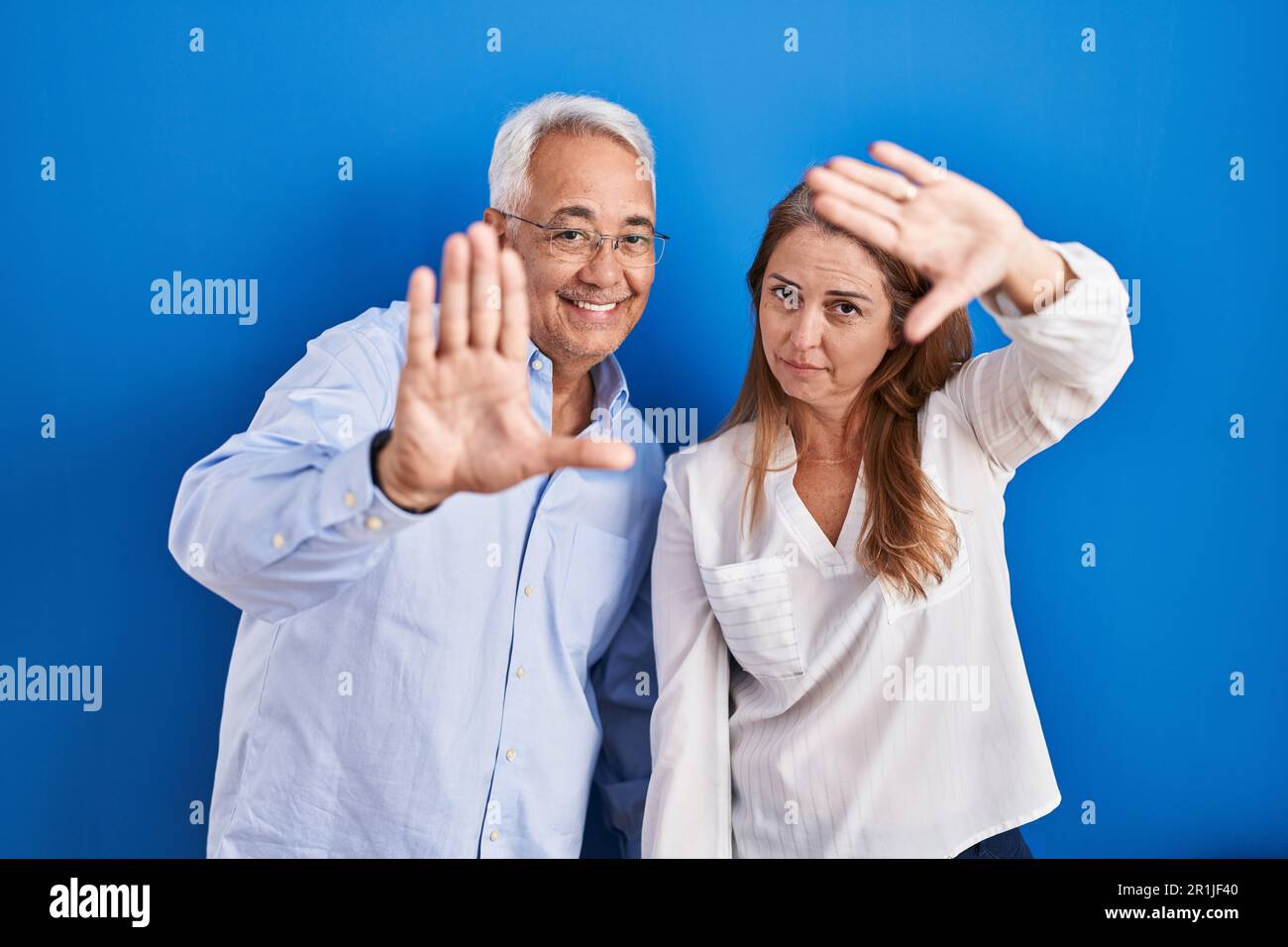 Middle age hispanic couple standing over blue background doing frame ...