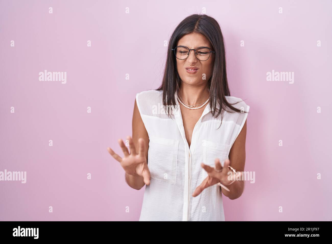 Brunette young woman standing over pink background wearing glasses ...