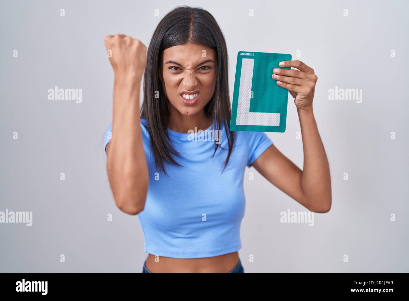 Brunette young woman holding l sign for new driver annoyed and ...
