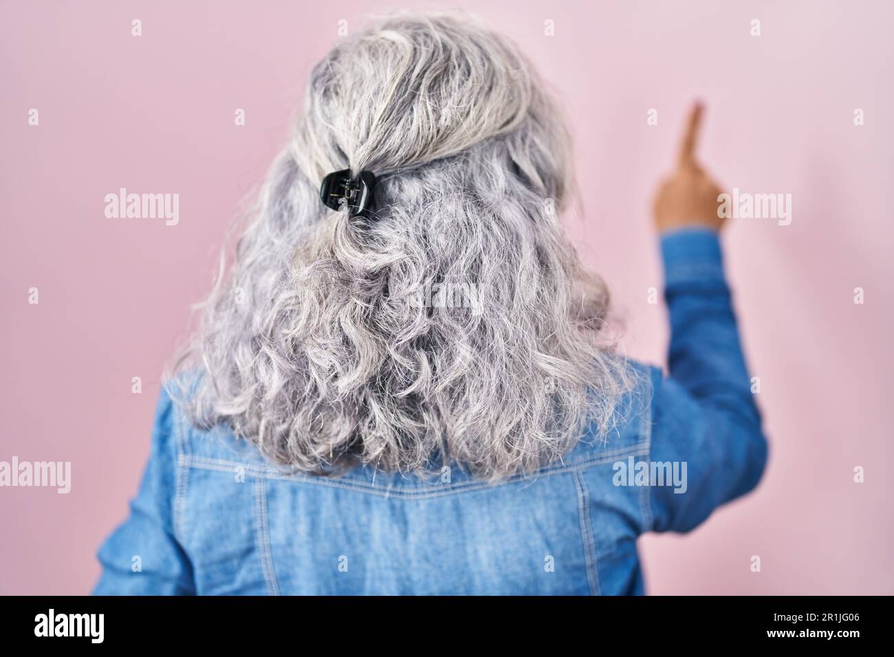 Middle age woman with grey hair standing over pink background posing ...