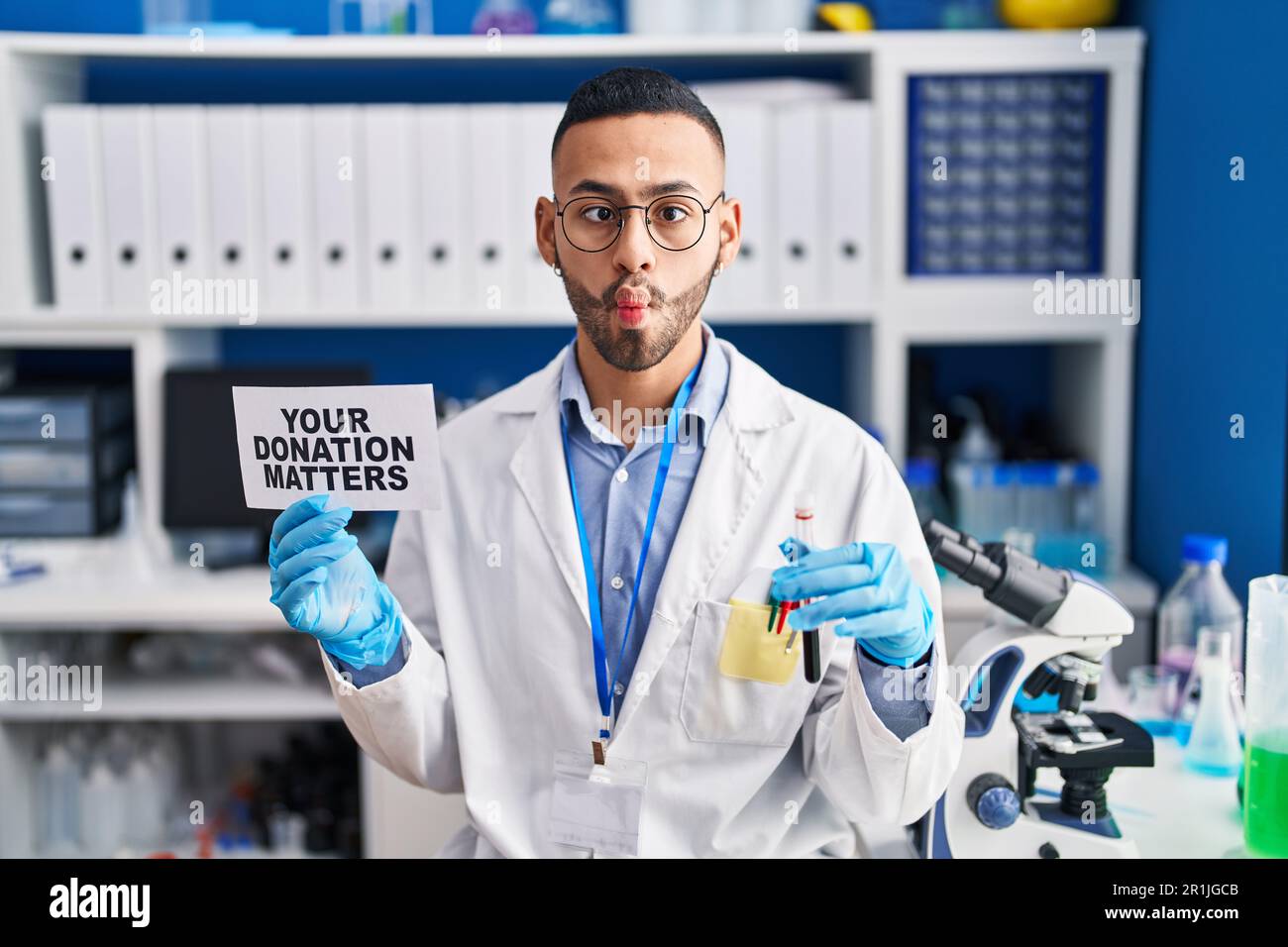 Young hispanic man working at scientist laboratory holding your donation matters holding blood ...