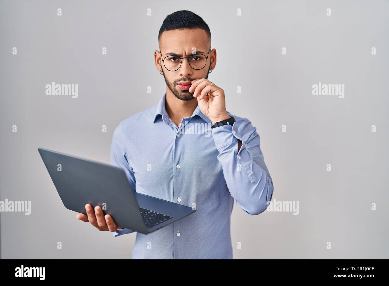 Young hispanic man working using computer laptop mouth and lips shut as ...