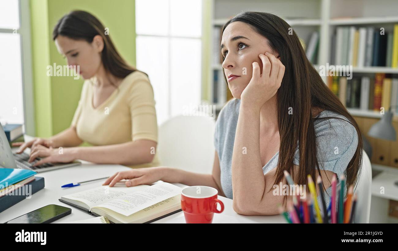 Two women sitting on table studying with boring expression at library ...
