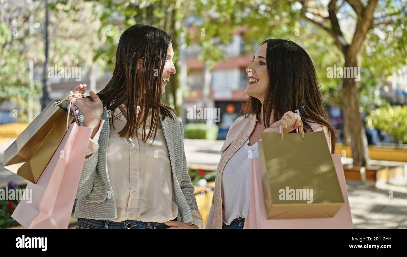 Two women smiling going shopping holding bags at park Stock Photo - Alamy