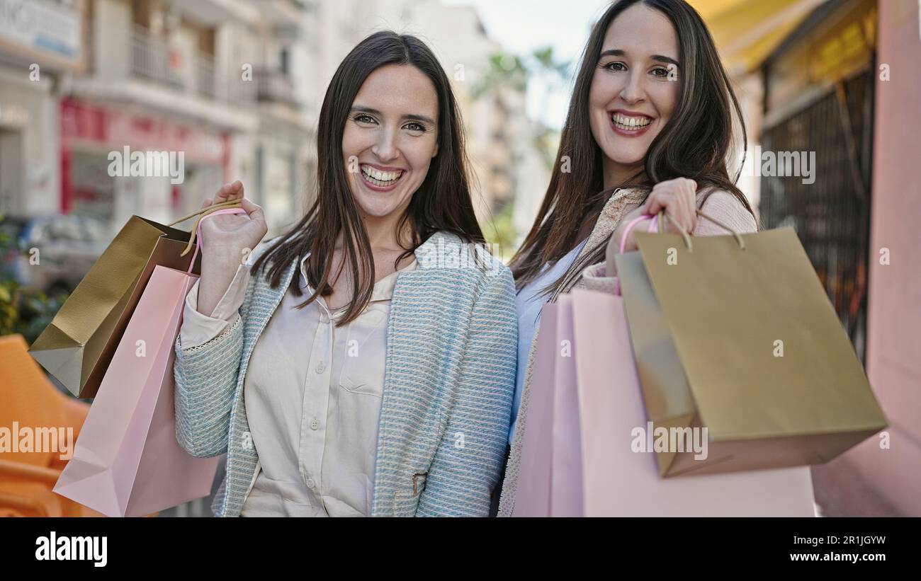 Two women smiling going shopping holding bags at street Stock Photo - Alamy
