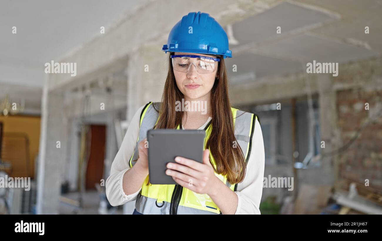 Young beautiful hispanic woman builder using touchpad at construction ...