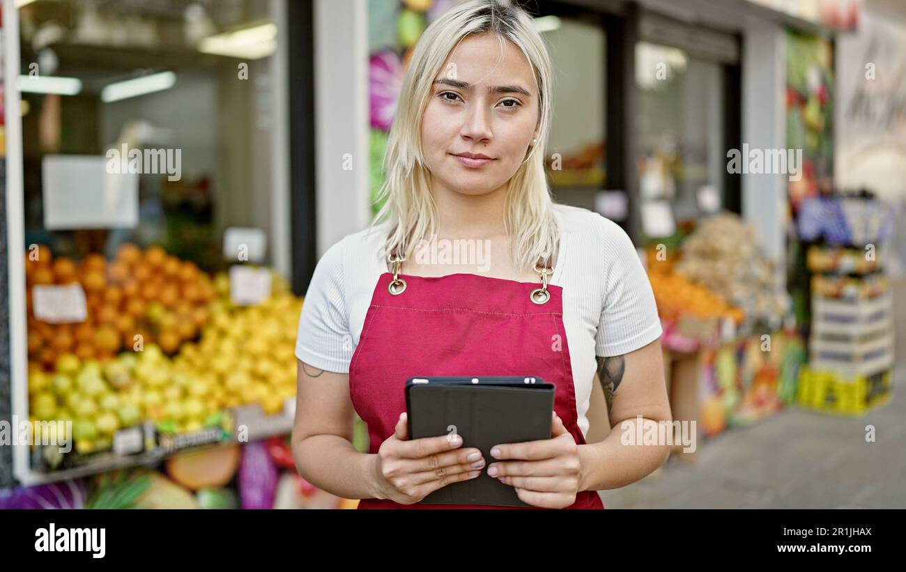 Young beautiful hispanic woman wearing apron using touchpad at fruit ...
