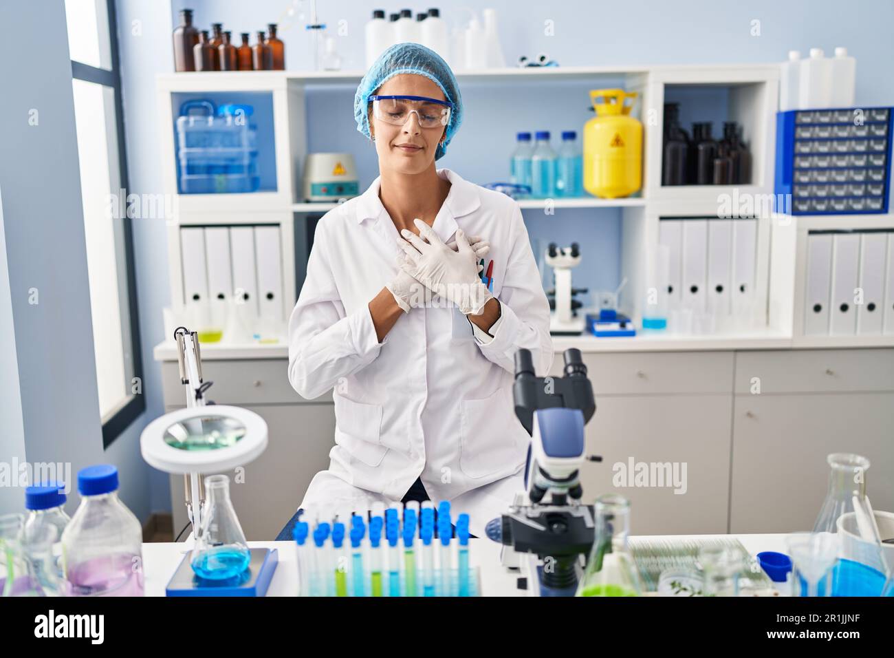 Brunette woman working at scientist laboratory smiling with hands on ...