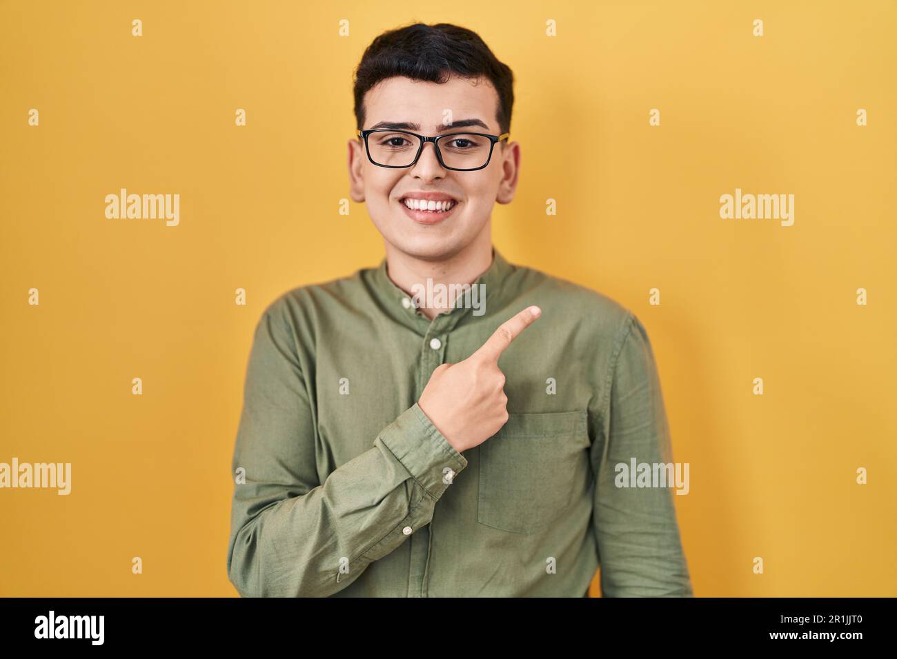 Non binary person standing over yellow background cheerful with a smile ...
