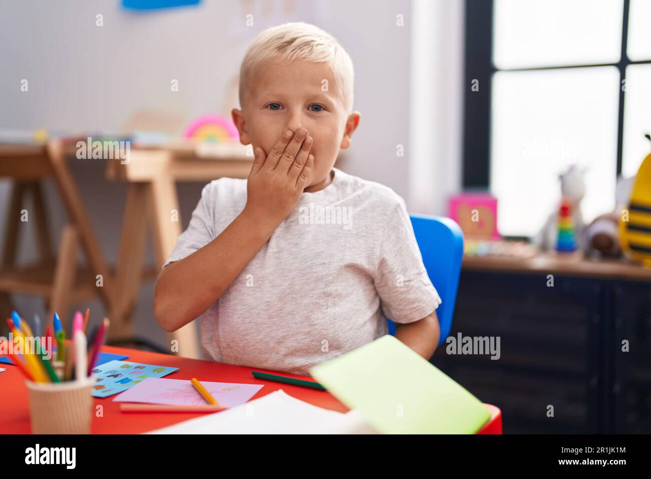 Little caucasian boy painting at the school covering mouth with hand ...