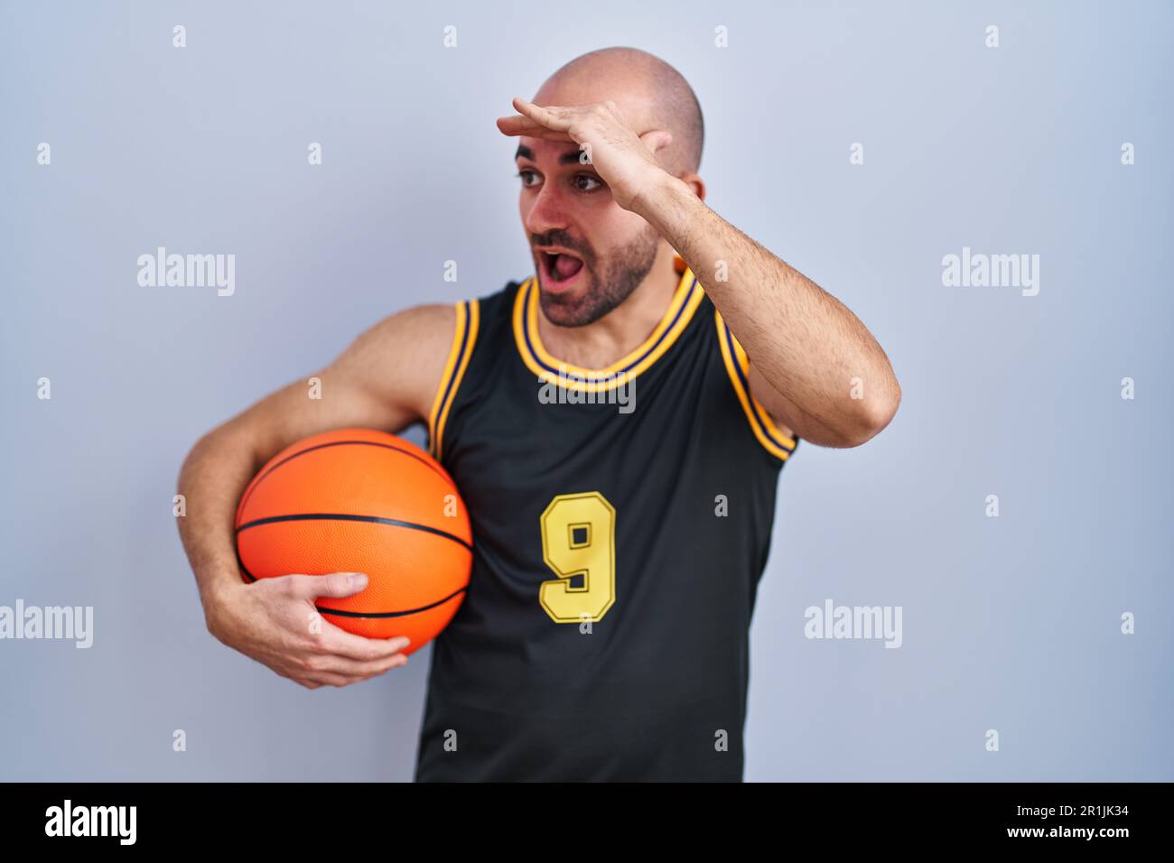Young bald man with beard wearing basketball uniform holding ball very ...