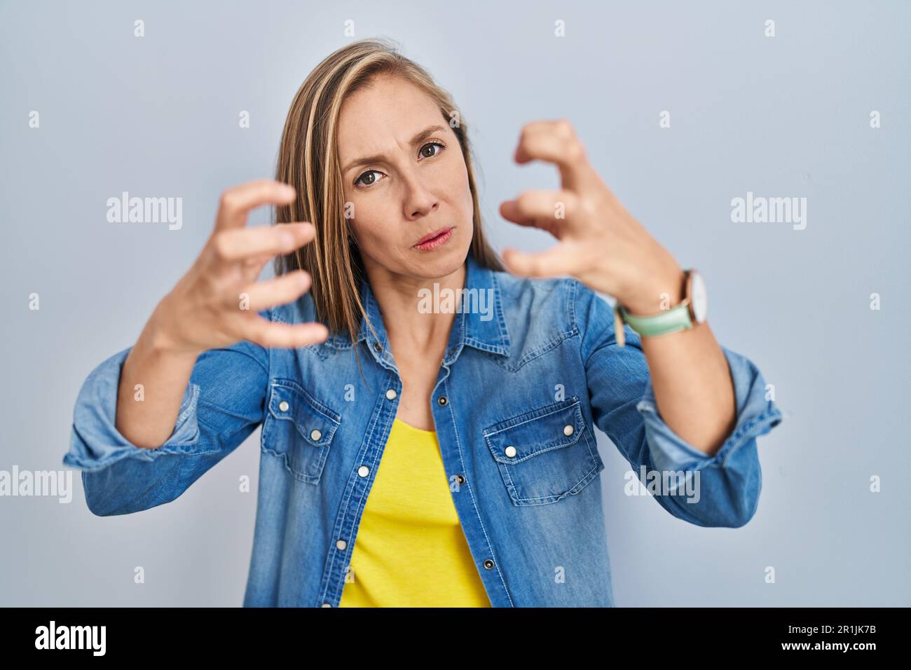 Young blonde woman standing over blue background shouting frustrated ...