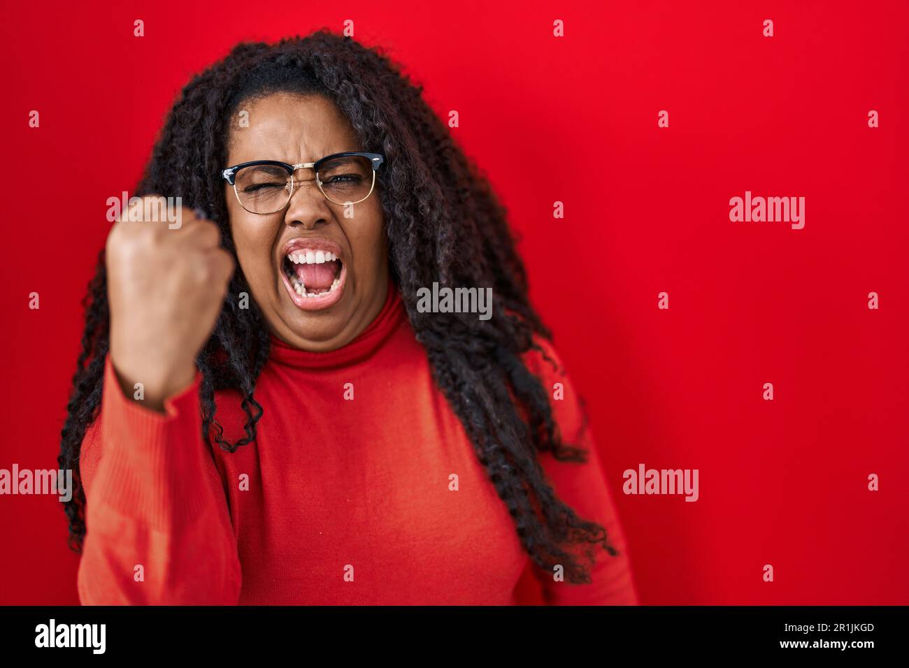 Plus size hispanic woman standing over red background angry and mad ...
