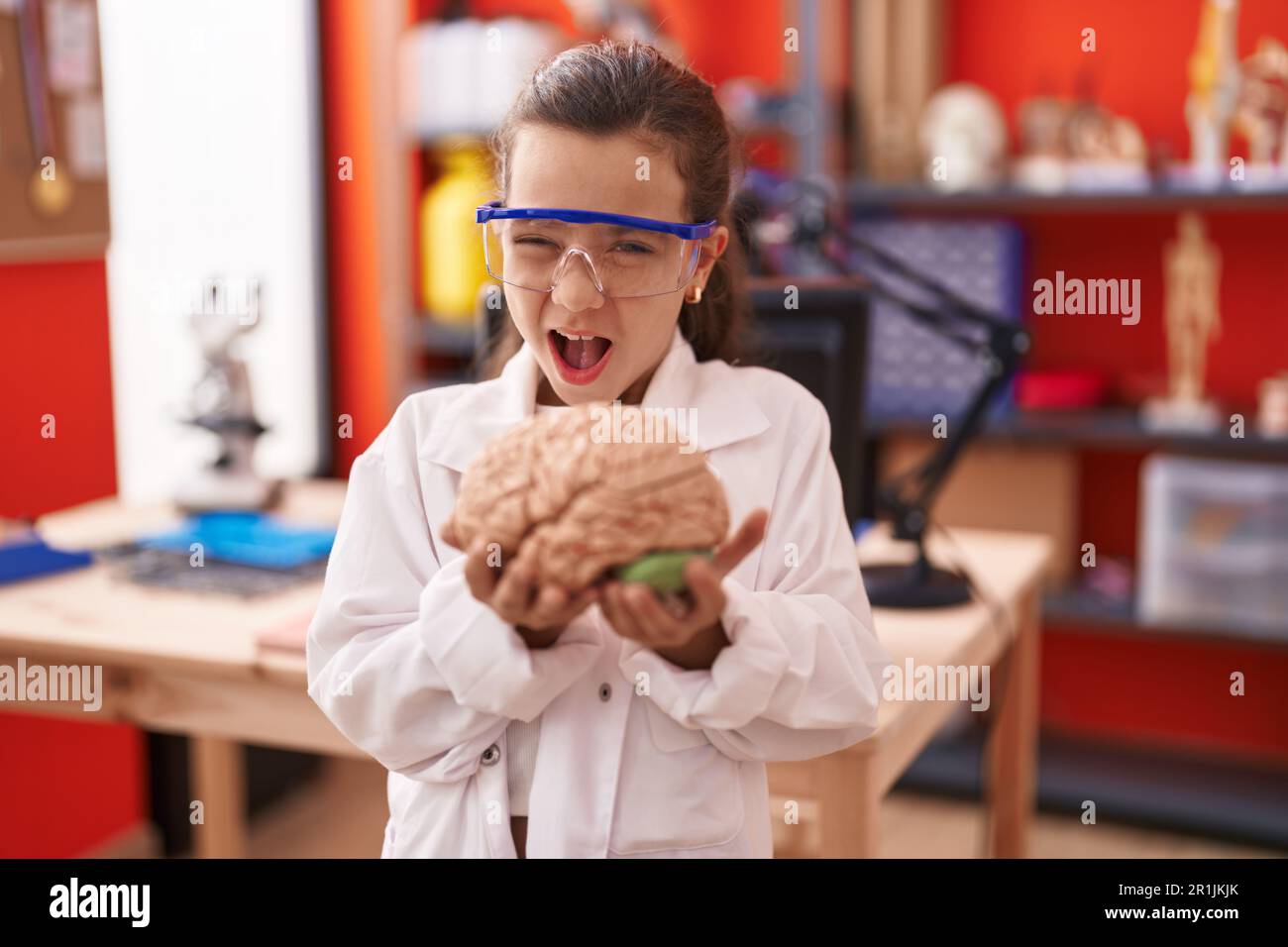 Little hispanic girl holding brain at science class at school angry and ...