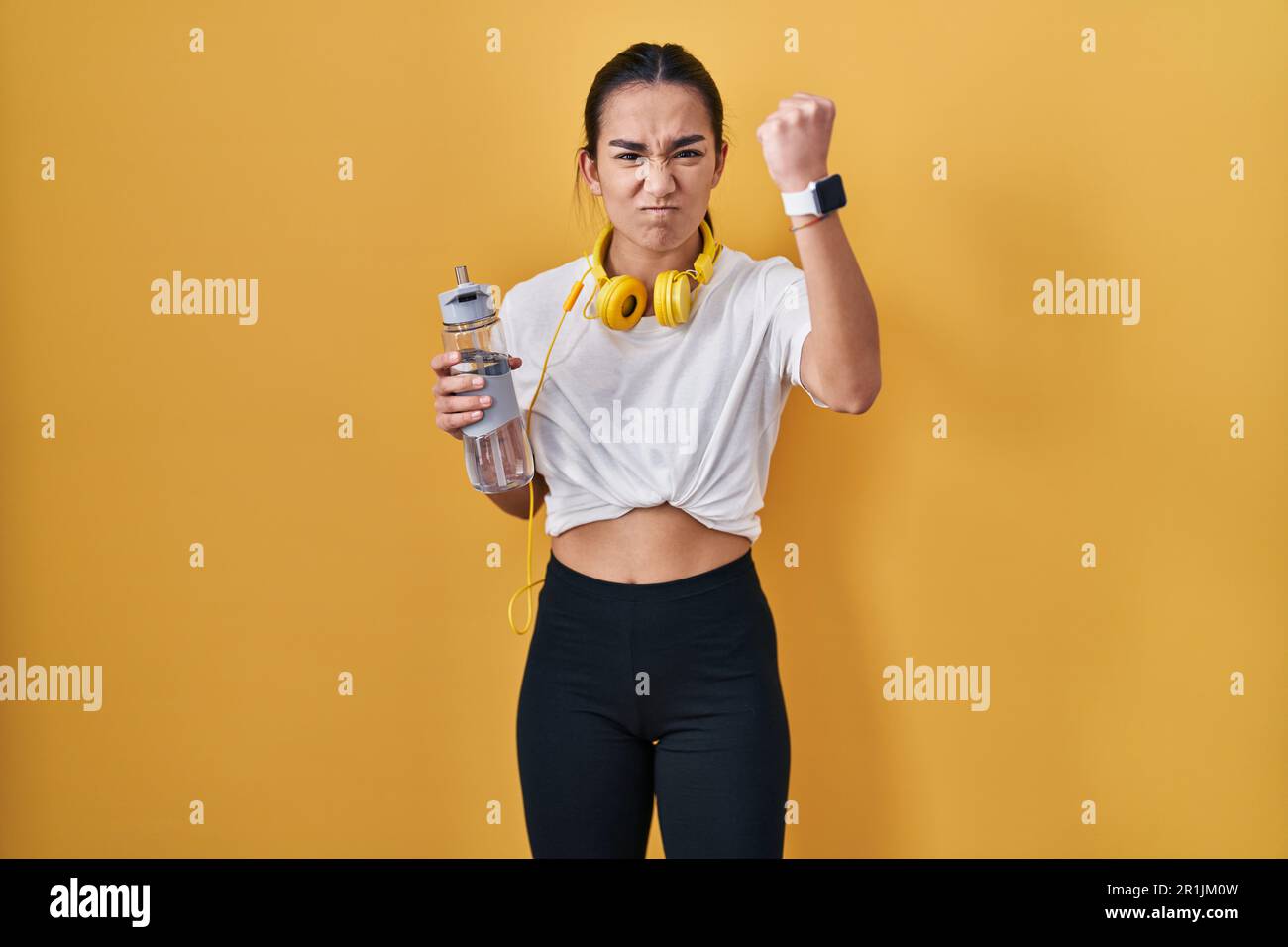 Young south asian woman wearing sportswear drinking water angry and mad ...