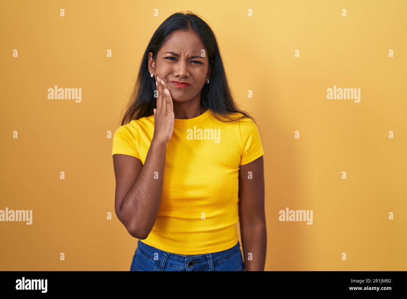 Young indian woman standing over yellow background touching mouth with ...
