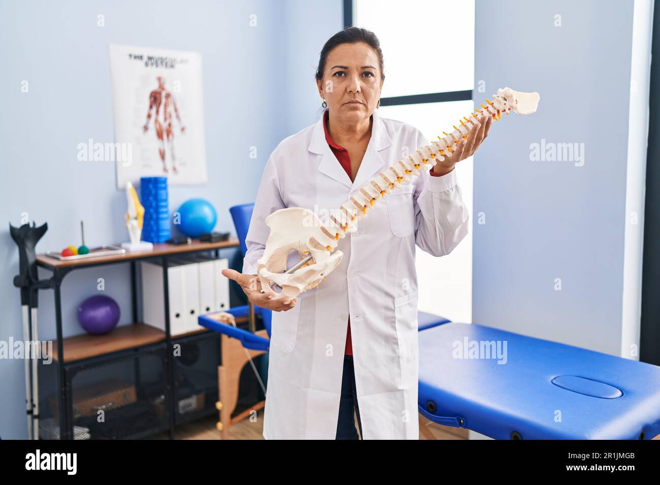 Middle age hispanic woman holding anatomical model of spinal column ...