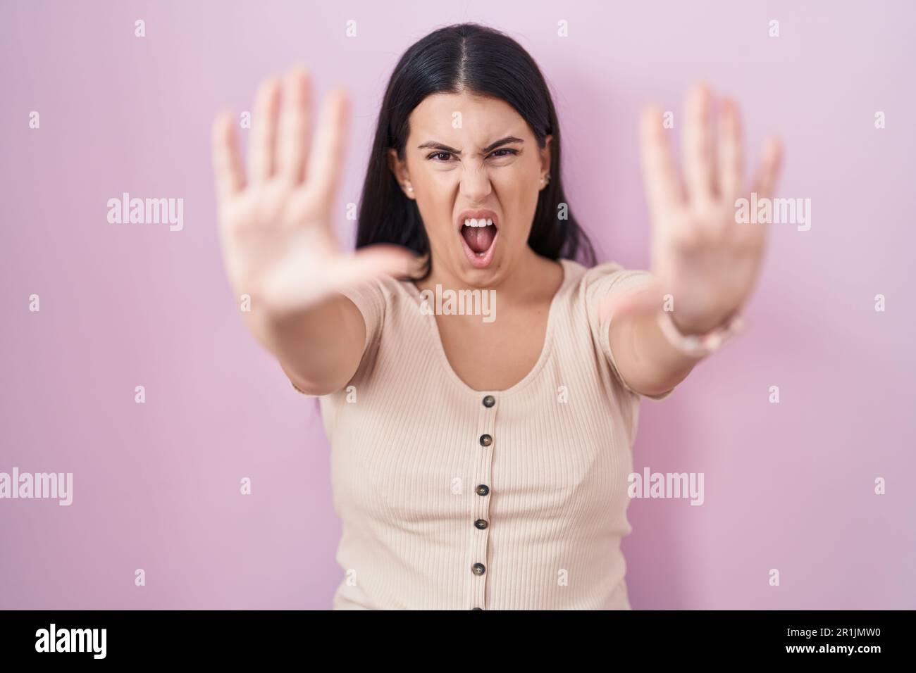 Young hispanic woman standing over pink background doing stop gesture ...