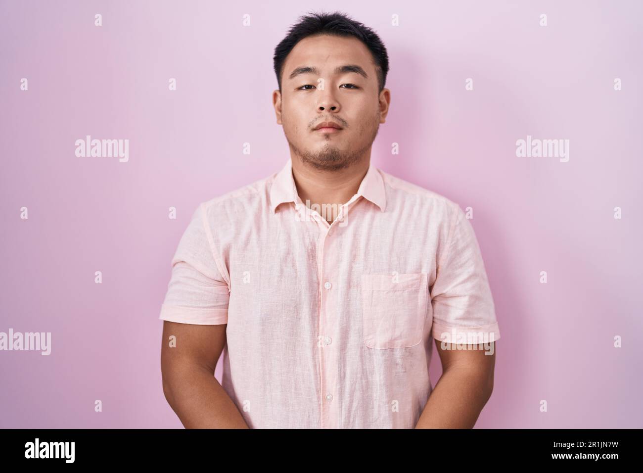 Chinese young man standing over pink background relaxed with serious ...