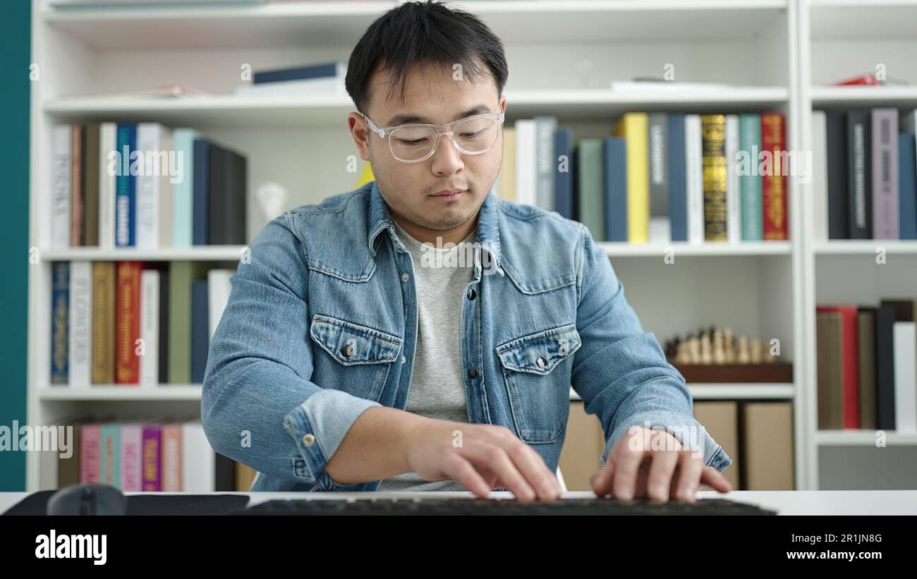 Young chinese man student using computer studying at library university ...