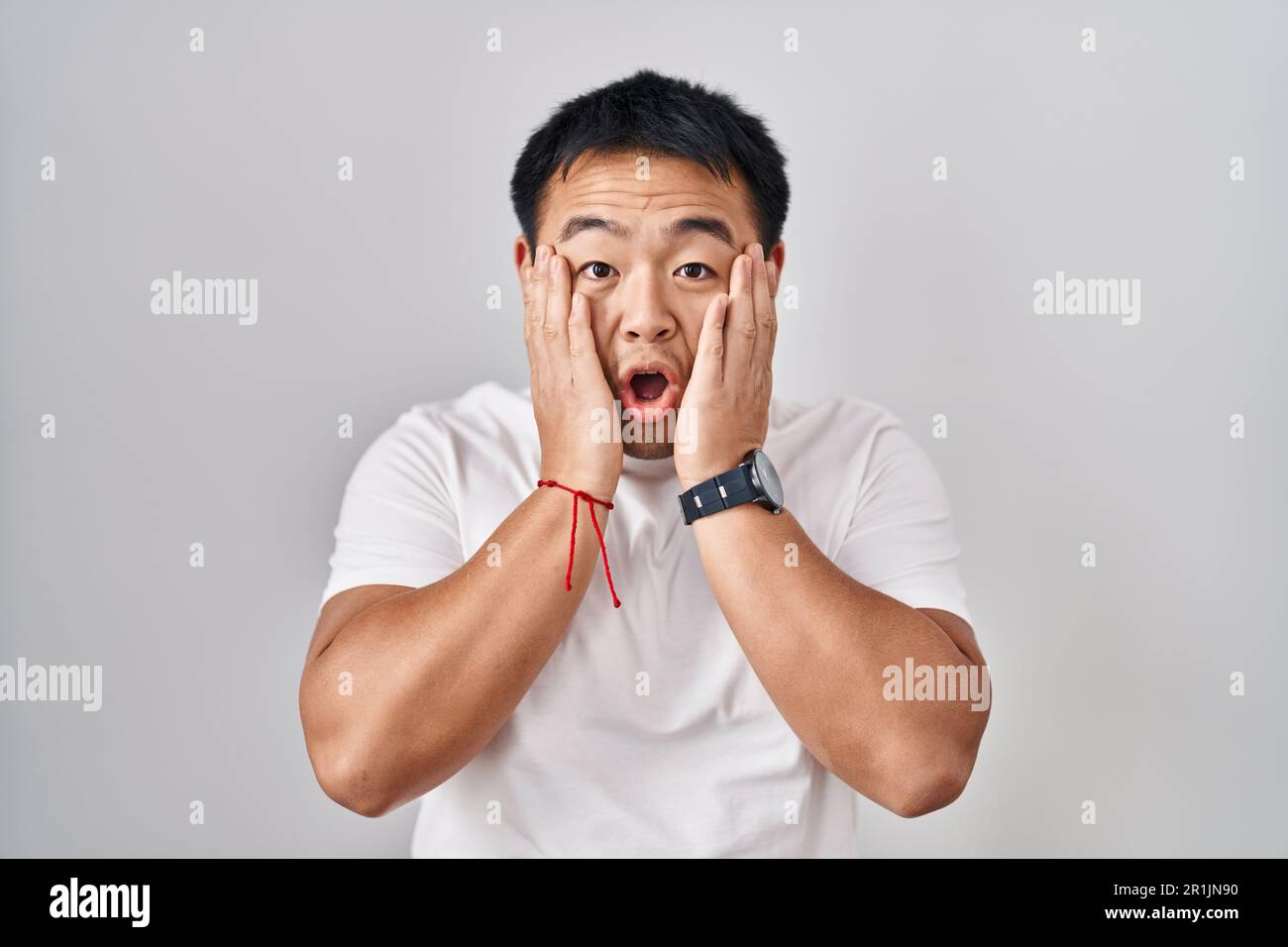 Young chinese man standing over white background afraid and shocked ...