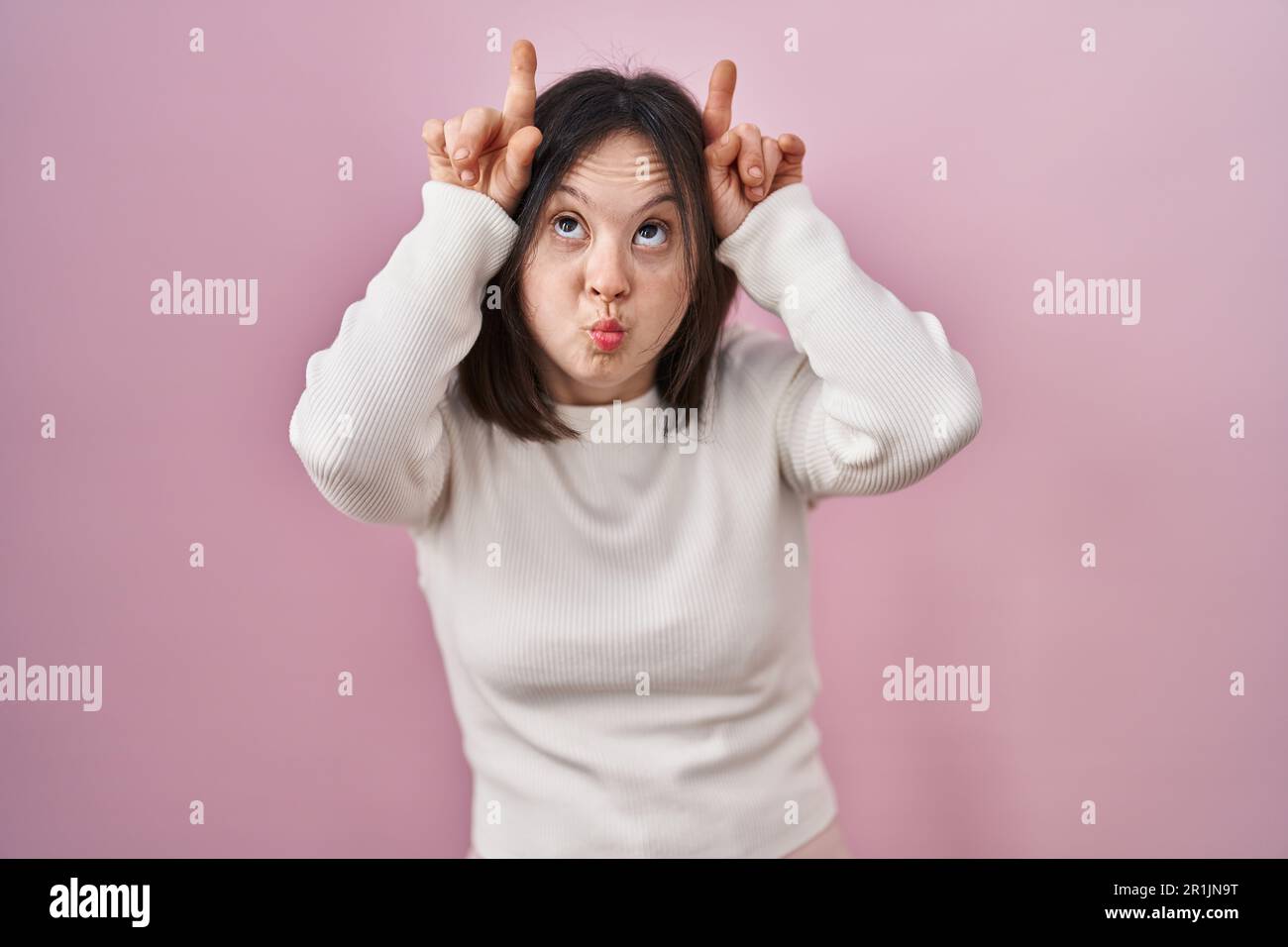 Woman with down syndrome standing over pink background doing funny ...