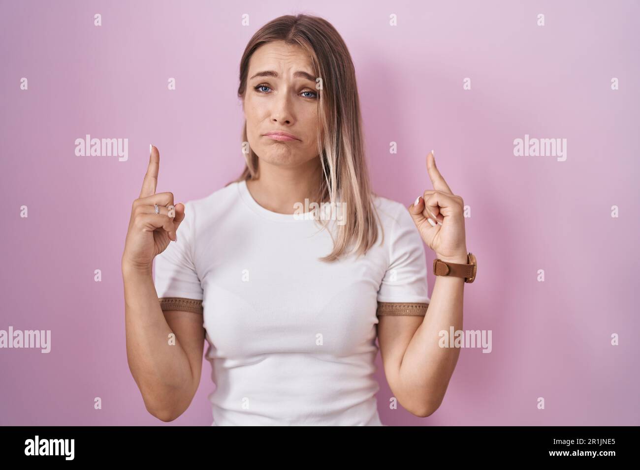 Blonde caucasian woman standing over pink background pointing up ...