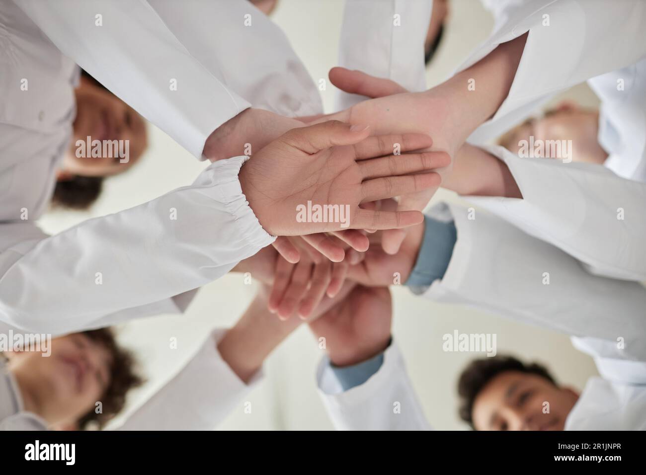Up view closeup of children stacking hands in science class and wearing ...