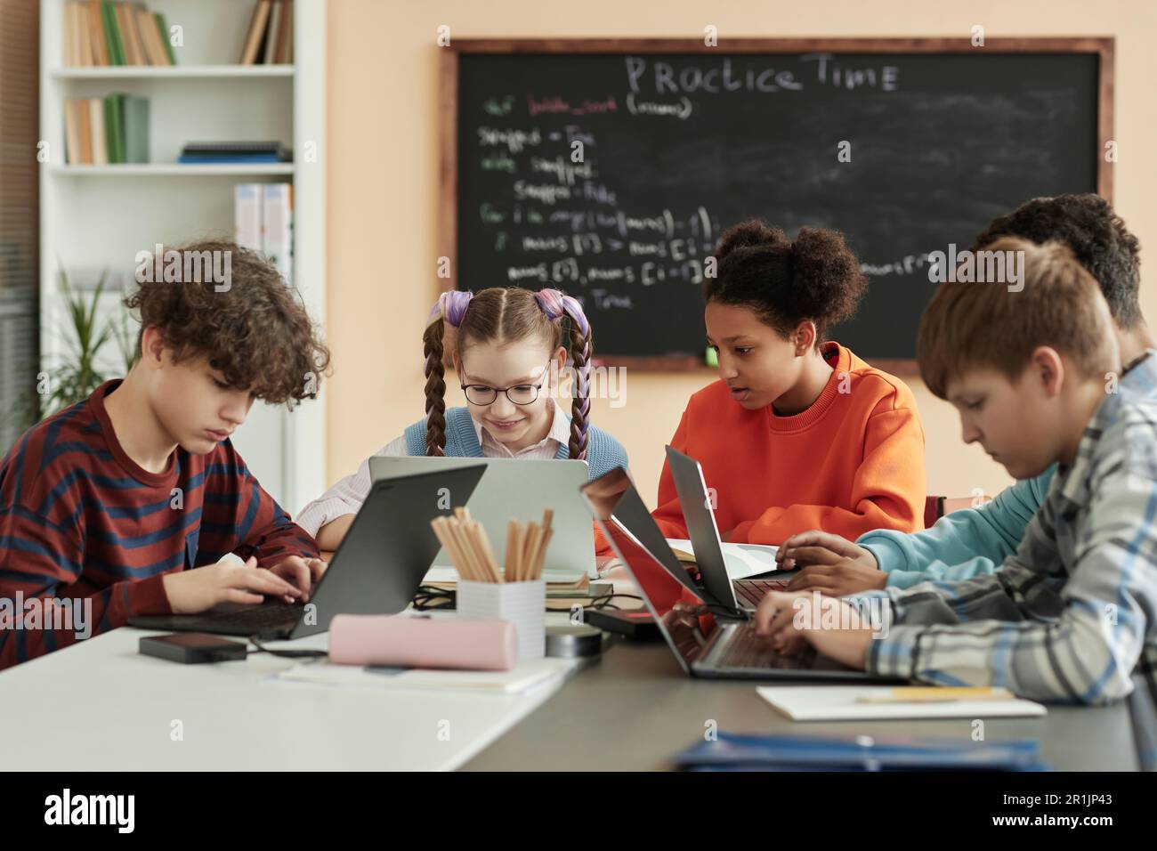 Diverse group of teen children using laptops in school classroom and ...