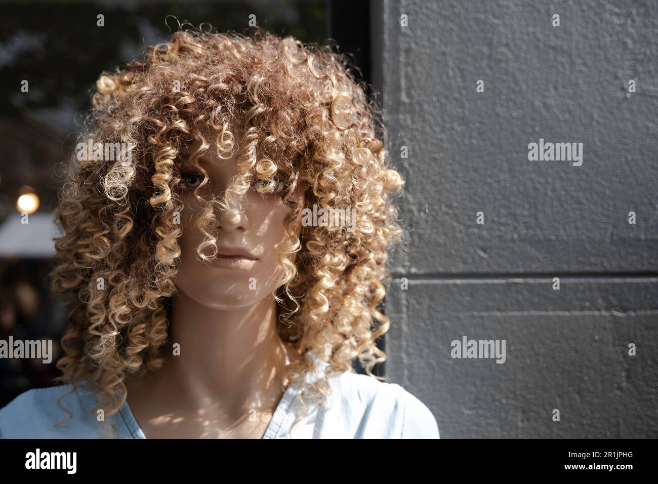 Plastic female mannequin with curly wig stands in front of the facade ...
