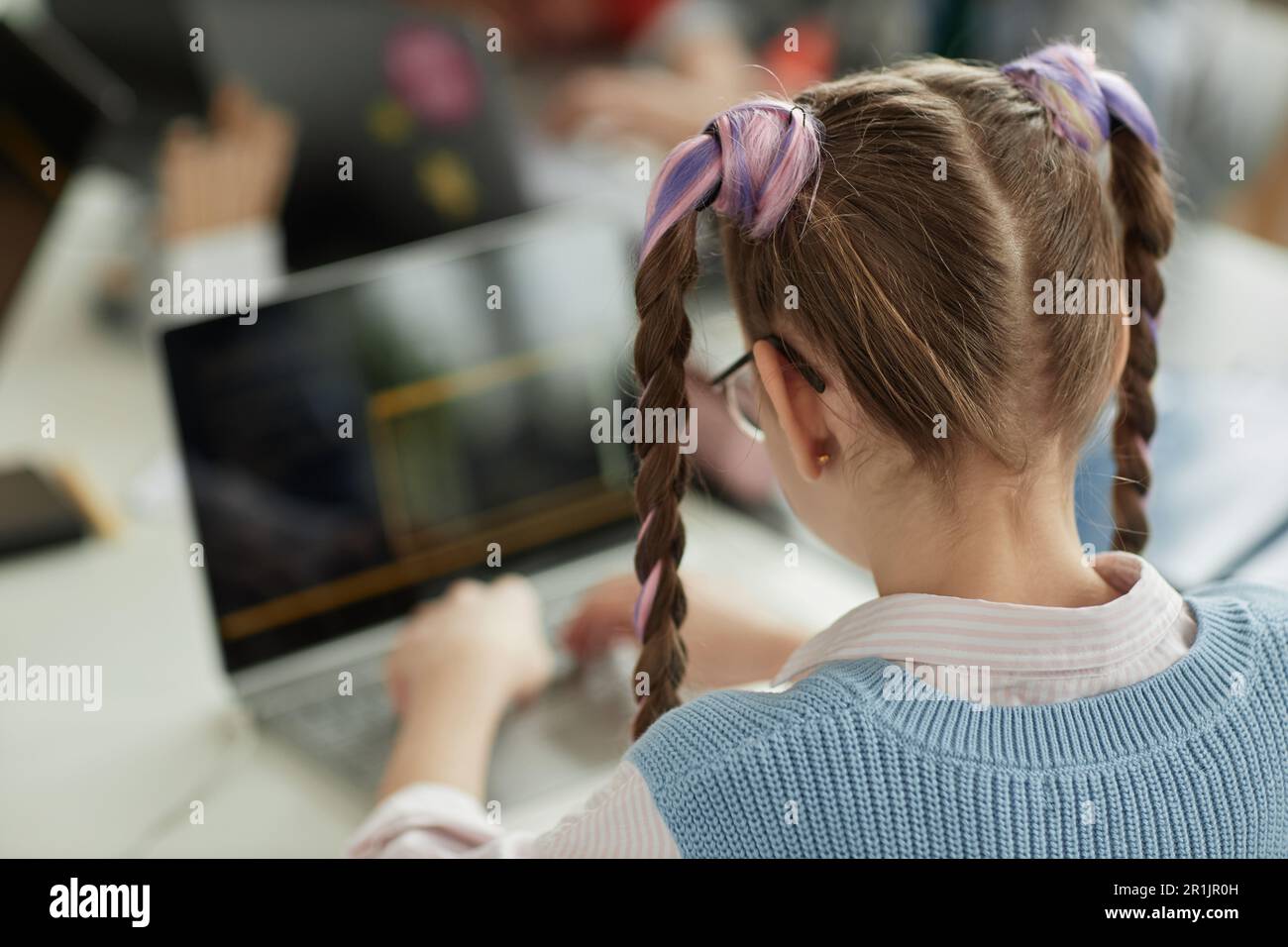 Back view at schoolgirl with cute pigtails using laptop in computer ...