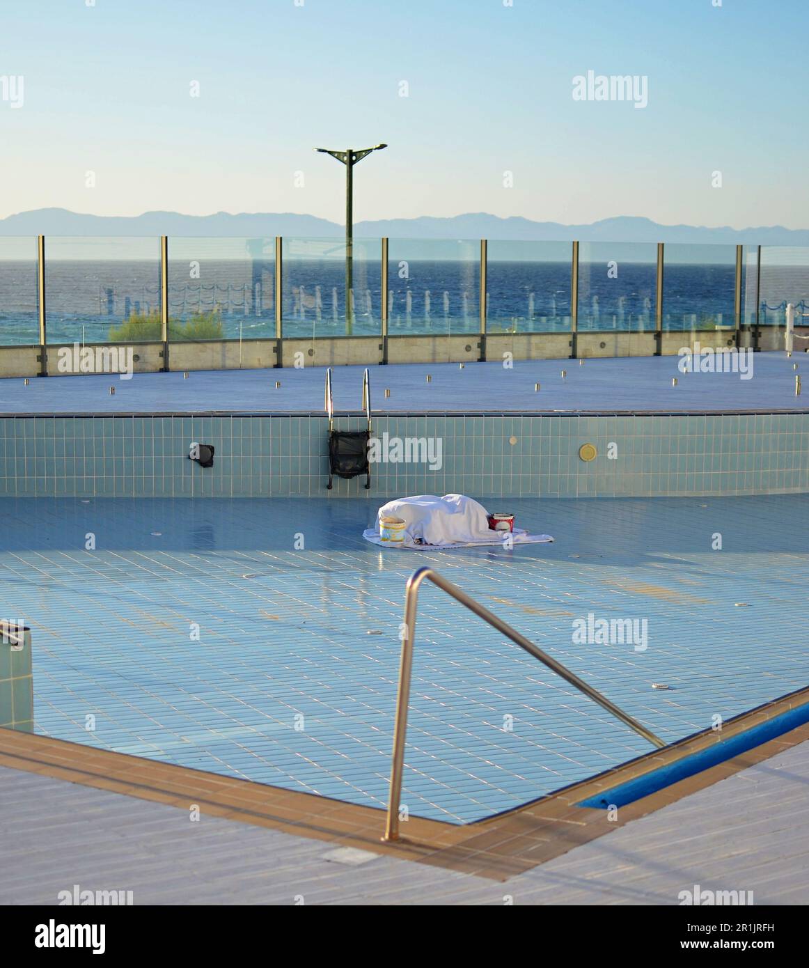 Empty swimming pool with blue tiles and glass fencing. Sea and ...