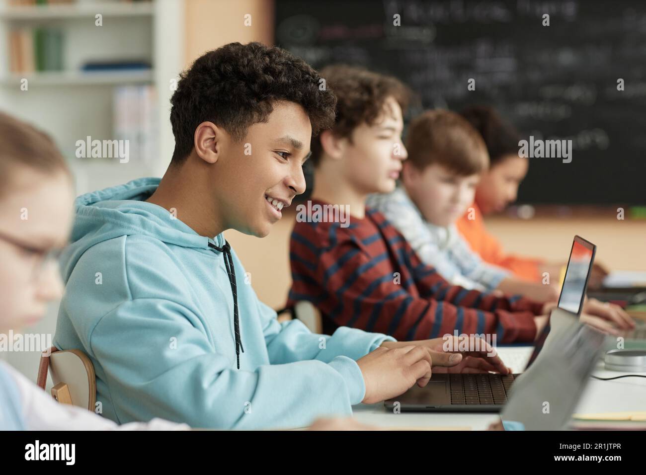 Side view at teen schoolboy using computer in row in school classroom ...