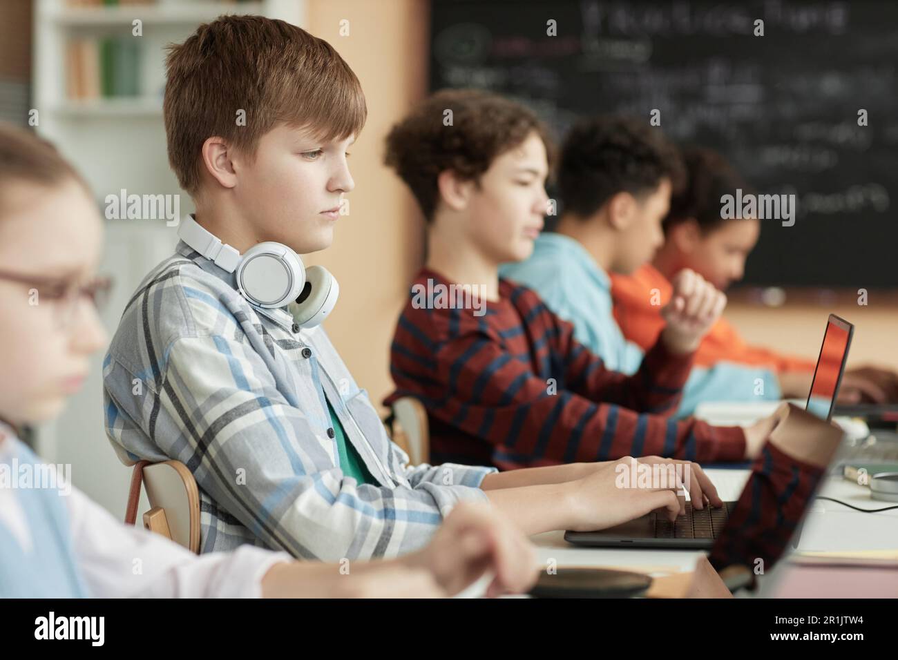 Side view at diverse group of children using computers in row in school ...