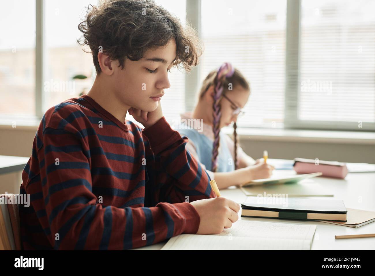 Side view portrait of teen boy with curly hair writing in notebook ...