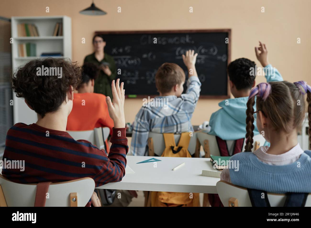 Back view at group of children raising hands in school classroom and ...