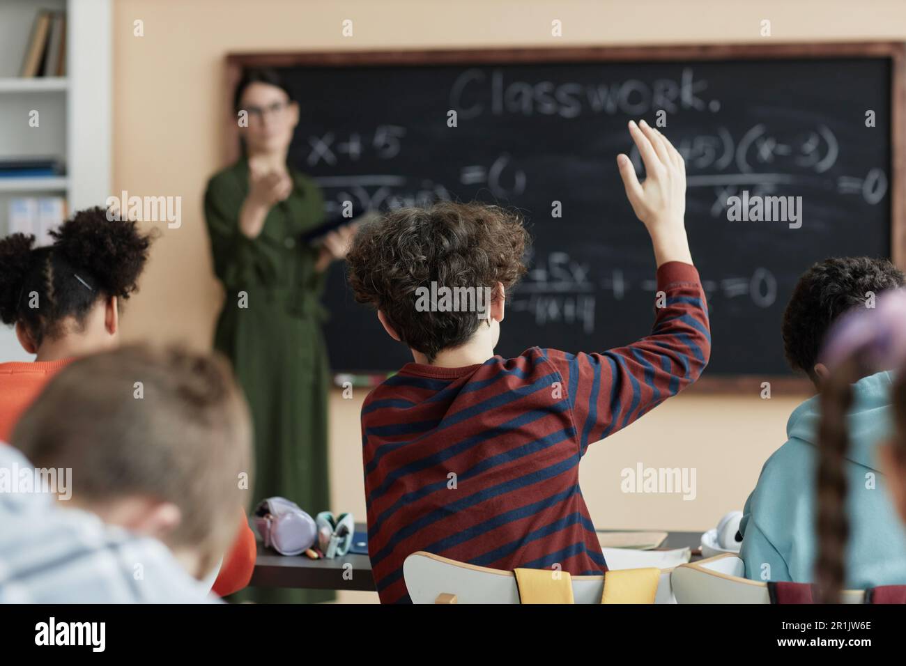 Back view at group of children raising hands in school classroom and ...
