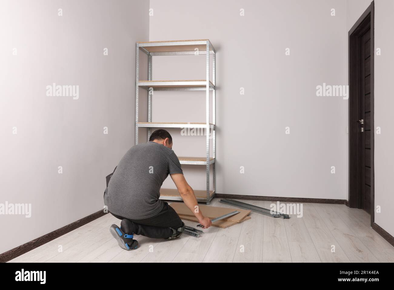 Worker assembling metal storage shelf in new office room, back view ...