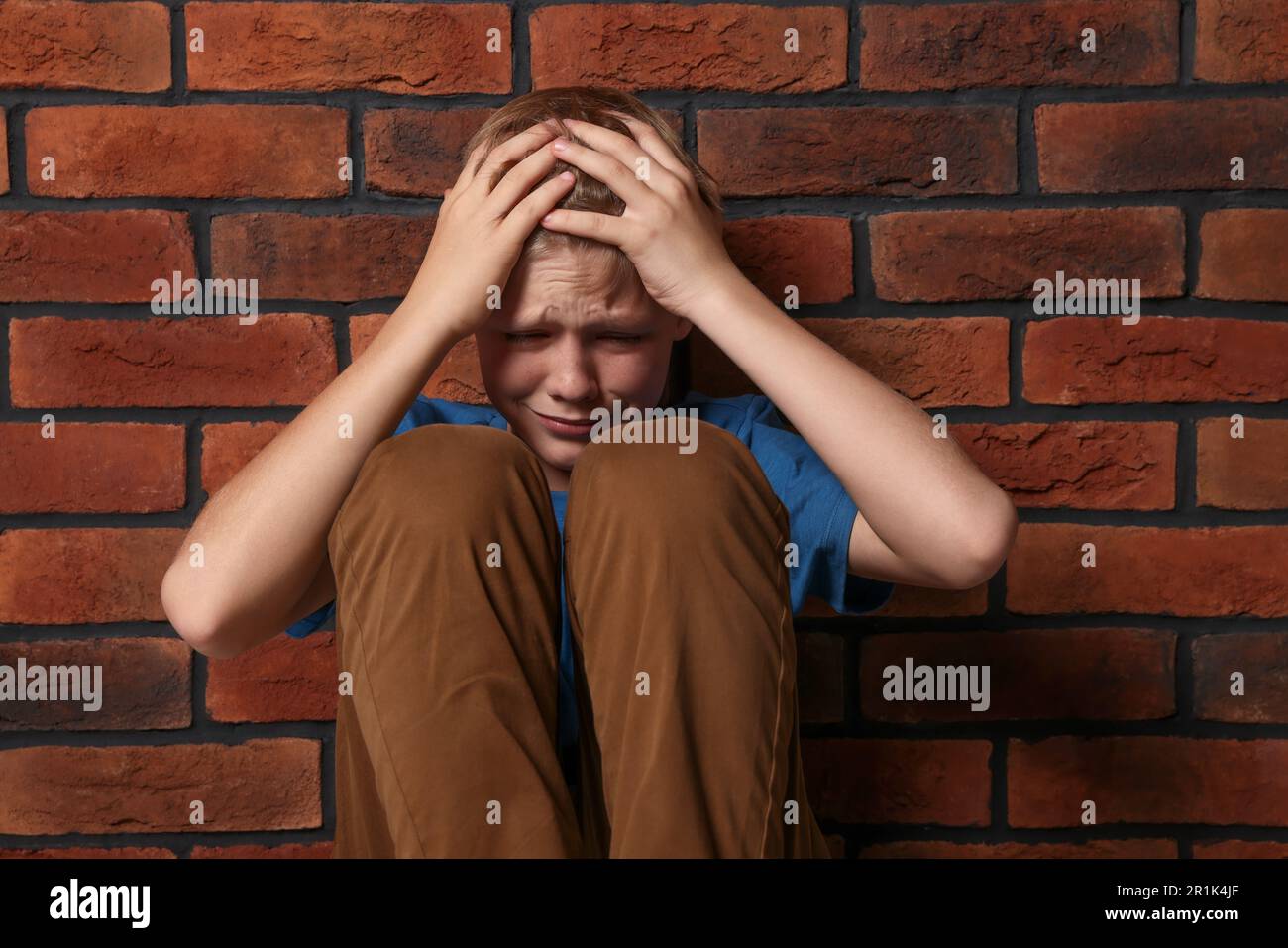 Upset boy sitting near brick wall. Children's bullying Stock Photo - Alamy