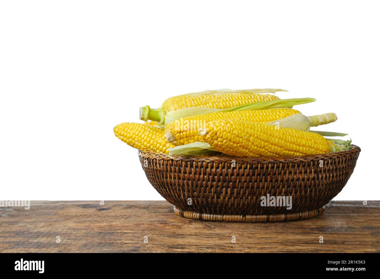 Tasty fresh corn cobs in wicker bowl on wooden table against white ...