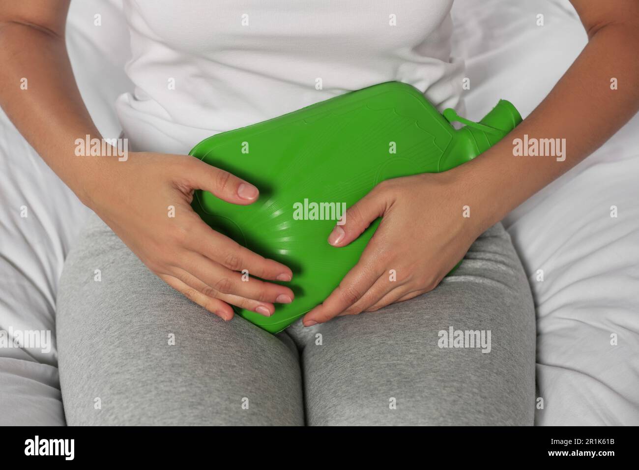 Young woman using hot water bottle to relieve cystitis pain on bed ...