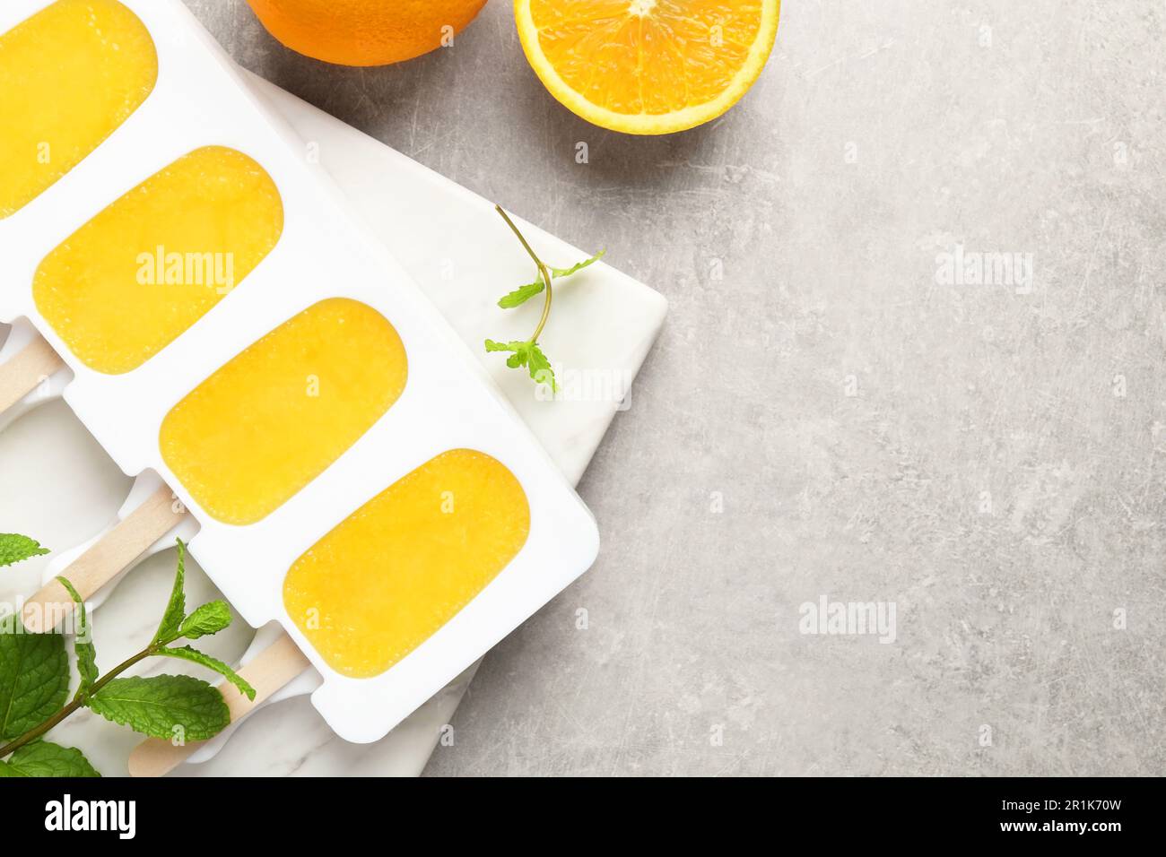 Tasty orange ice pops in mold and space for text on light grey table ...