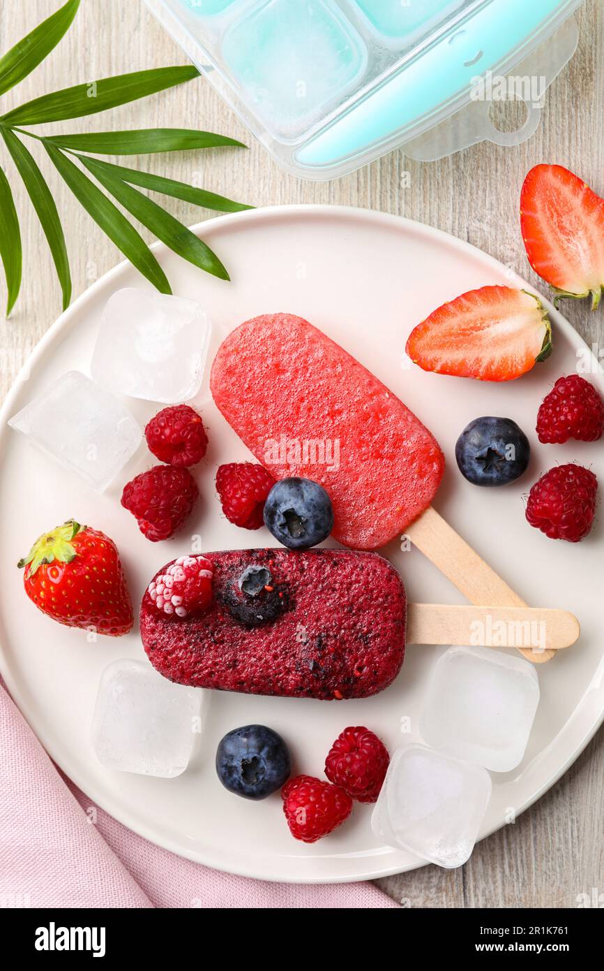 Plate of tasty berry ice pops on light wooden table, flat lay. Fruit ...