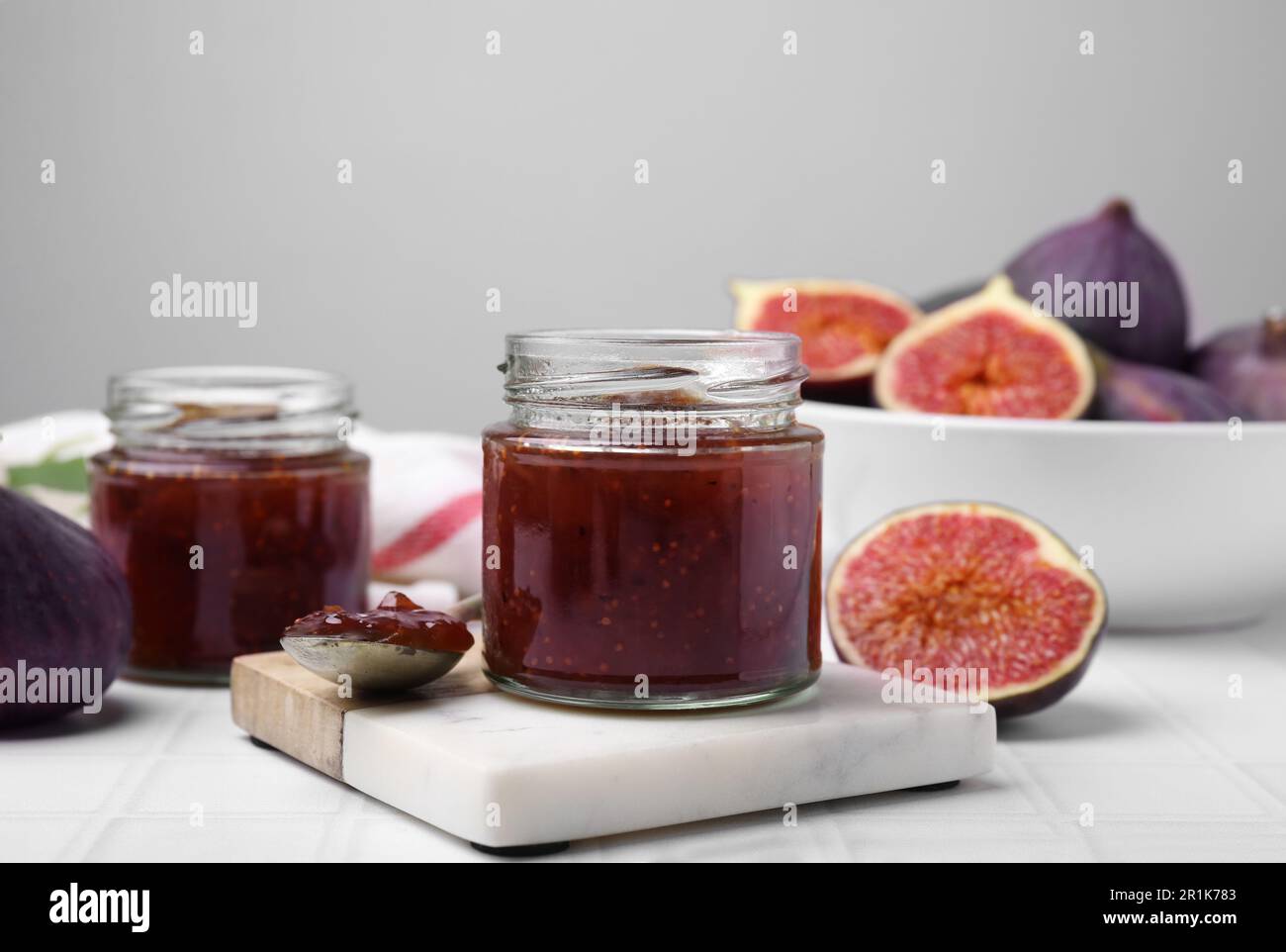 Glass jars of tasty sweet fig jam and fruits on white tiled table Stock ...