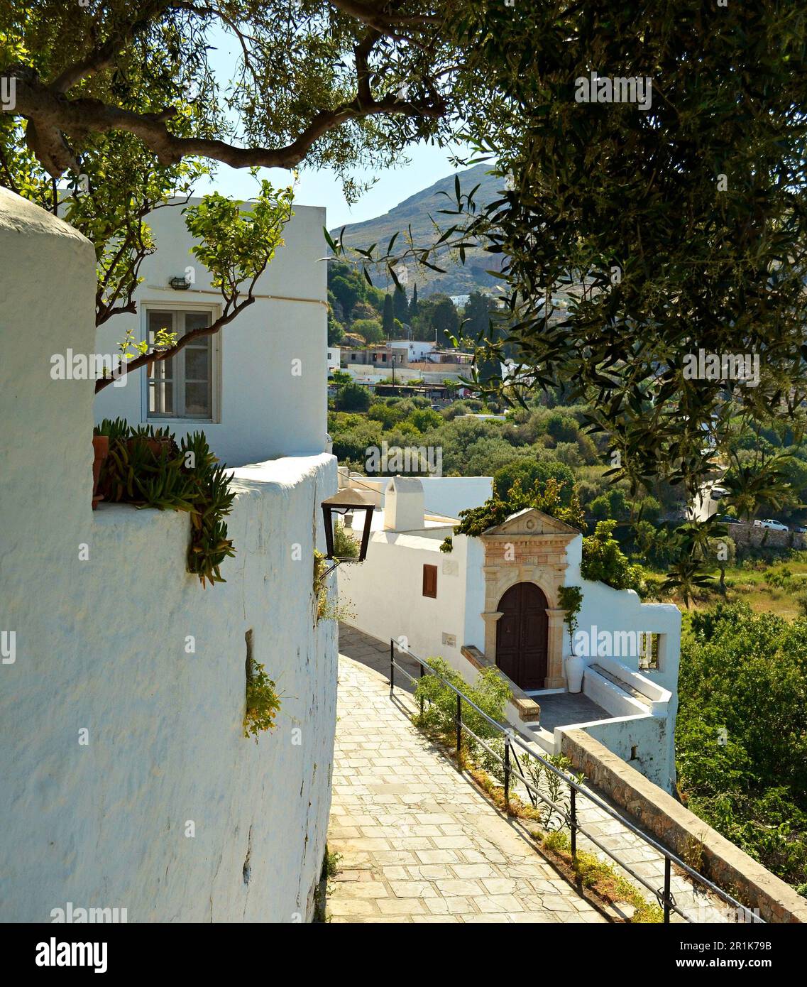 A narrow street in the Greek village of Lindos, with white walls, leads ...